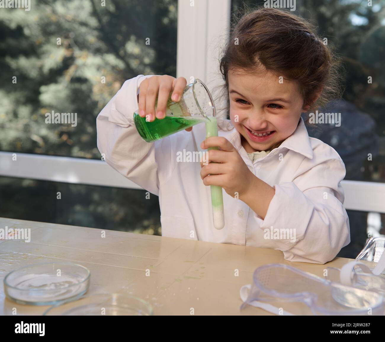 Delightful preschooler girl pouring solution from a beaker into a test ...