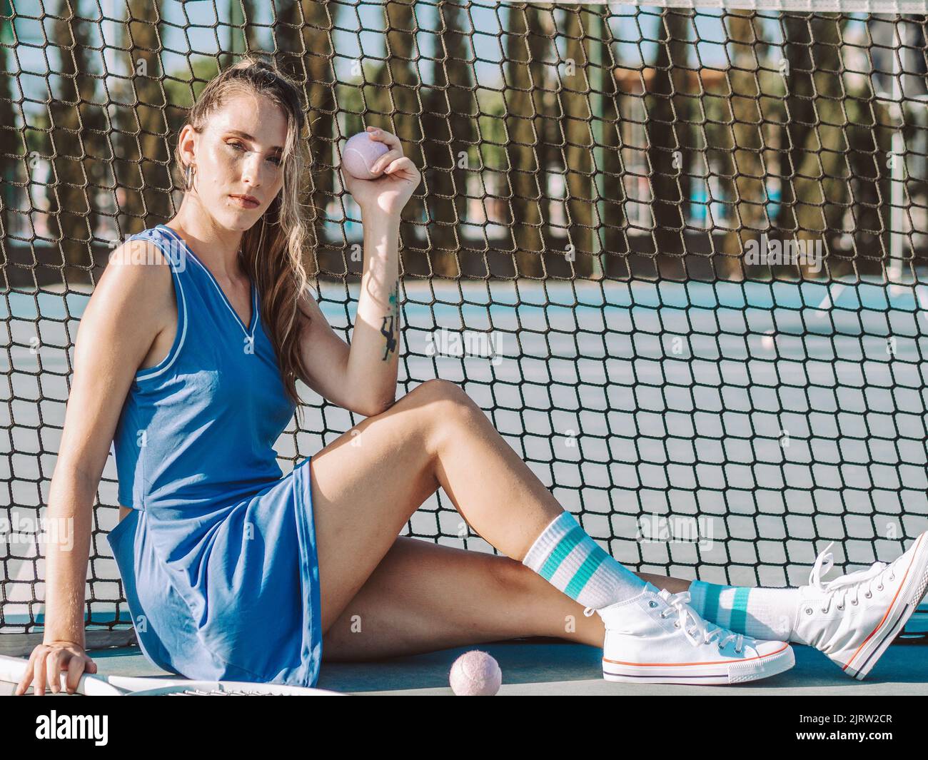 A female tennis player sitting on court ground with a ball in her hand ...