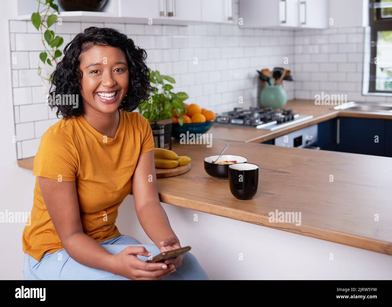 A young multi-ethnic woman texts while eating breakfast in the kitchen ...