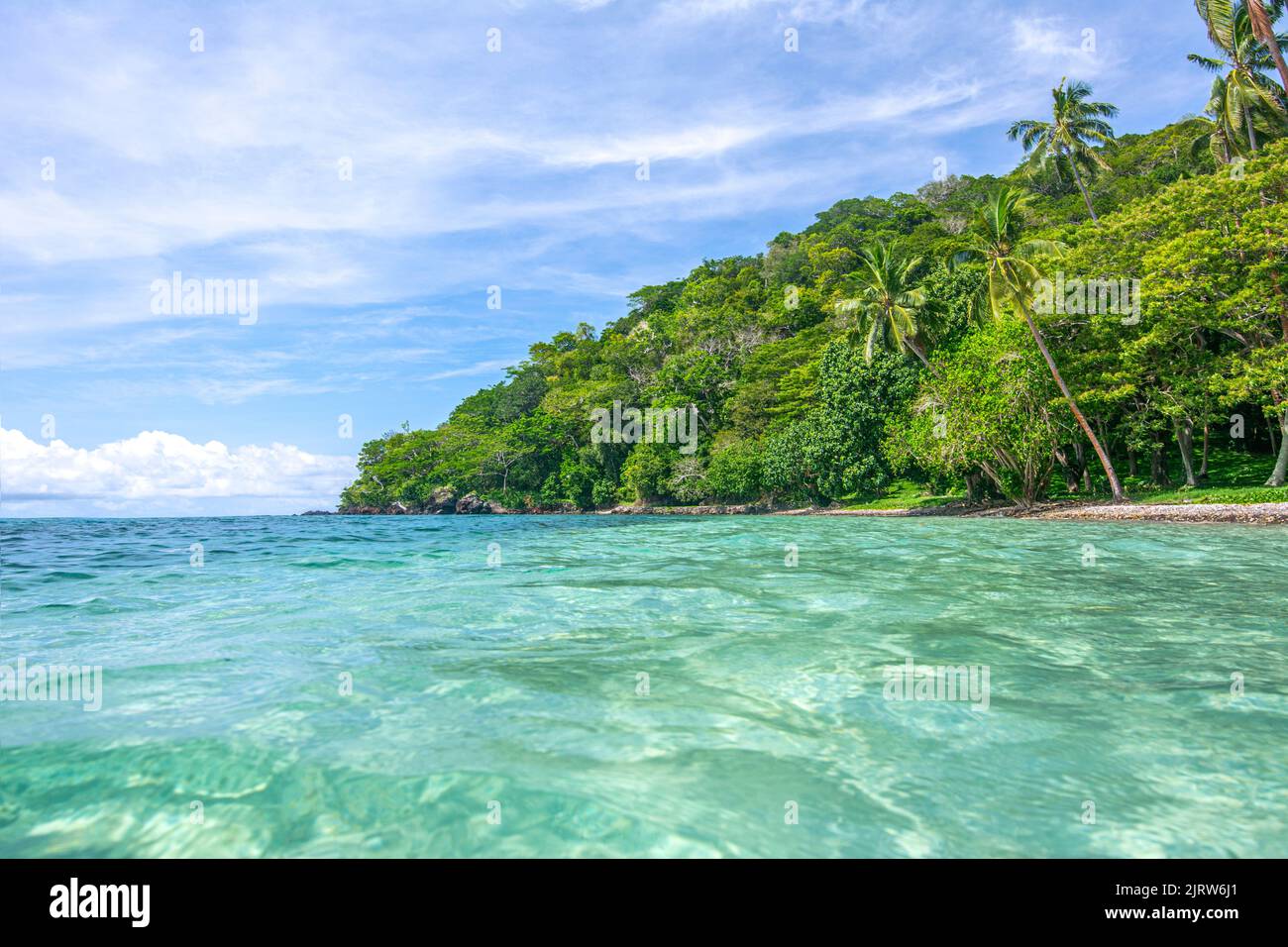 A beautiful tropical beach shows the clear water, lush island and ...