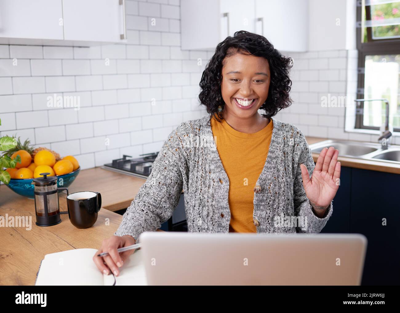 A young multi-ethnic woman greets her colleagues working from kitchen ...
