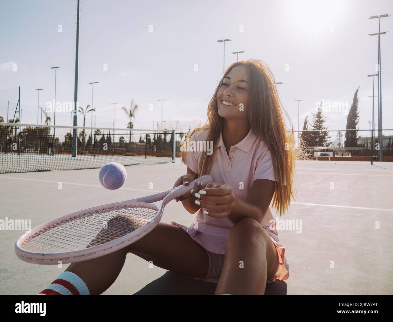 A female tennis player sitting on court ground and playing with racket ...