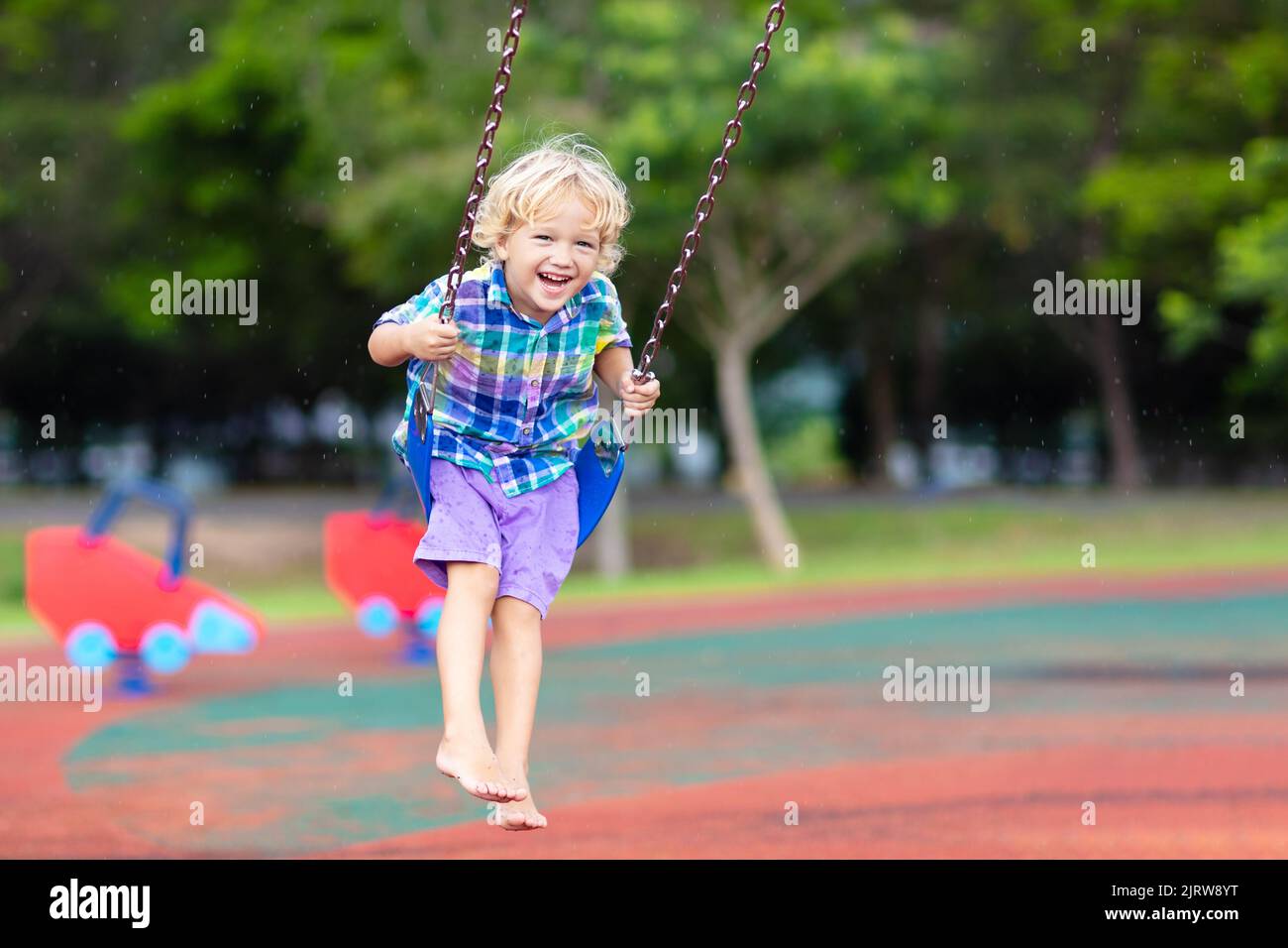 Child playing on outdoor playground in rain. Kids play on school or ...