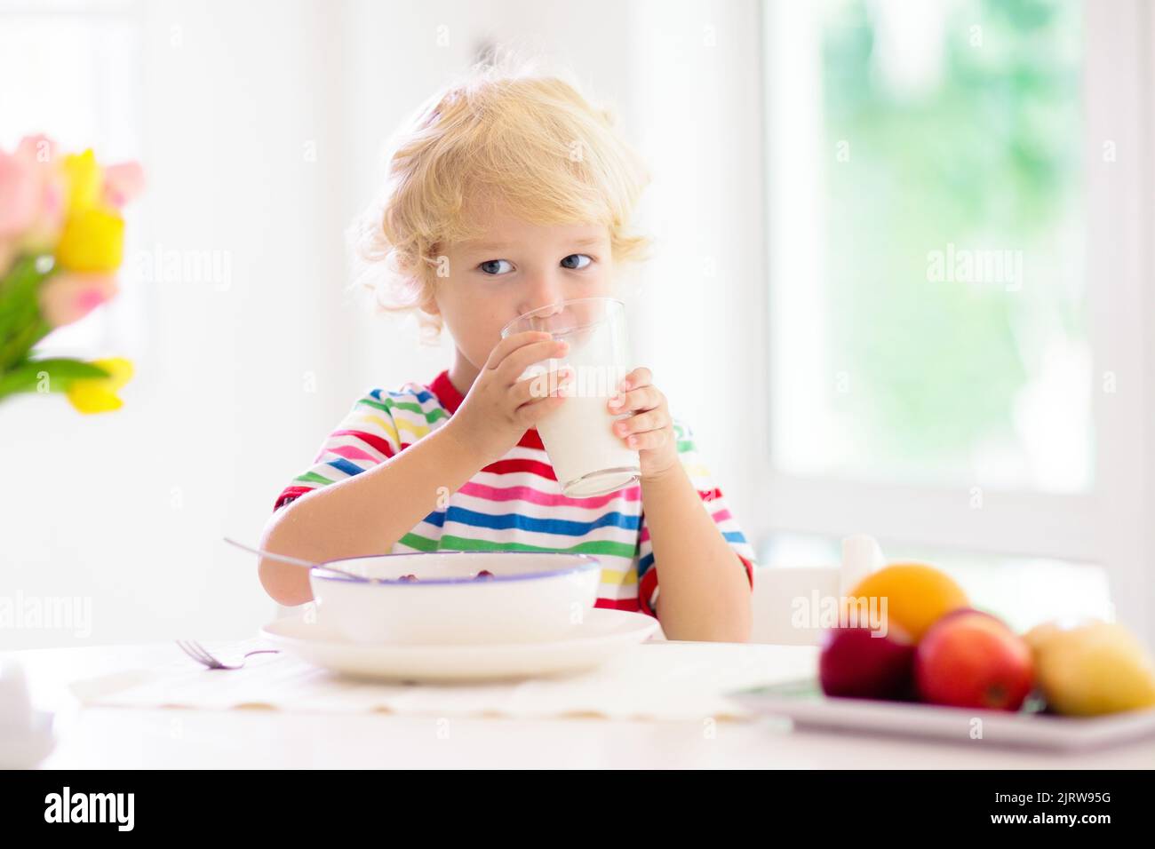 Child having breakfast. Kid drinking milk and eating cereal with fruit ...