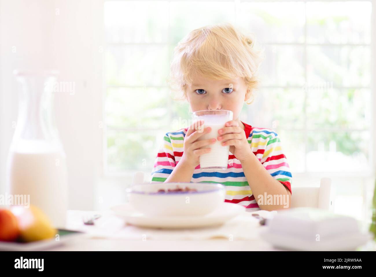 Child having breakfast. Kid drinking milk and eating cereal with fruit ...