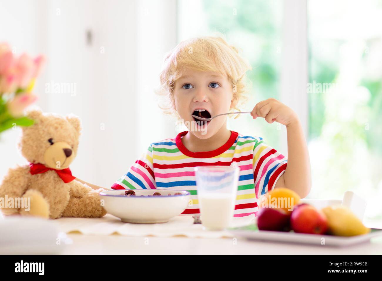 Child having breakfast. Kid feeding teddy bear toy, drinking milk and ...