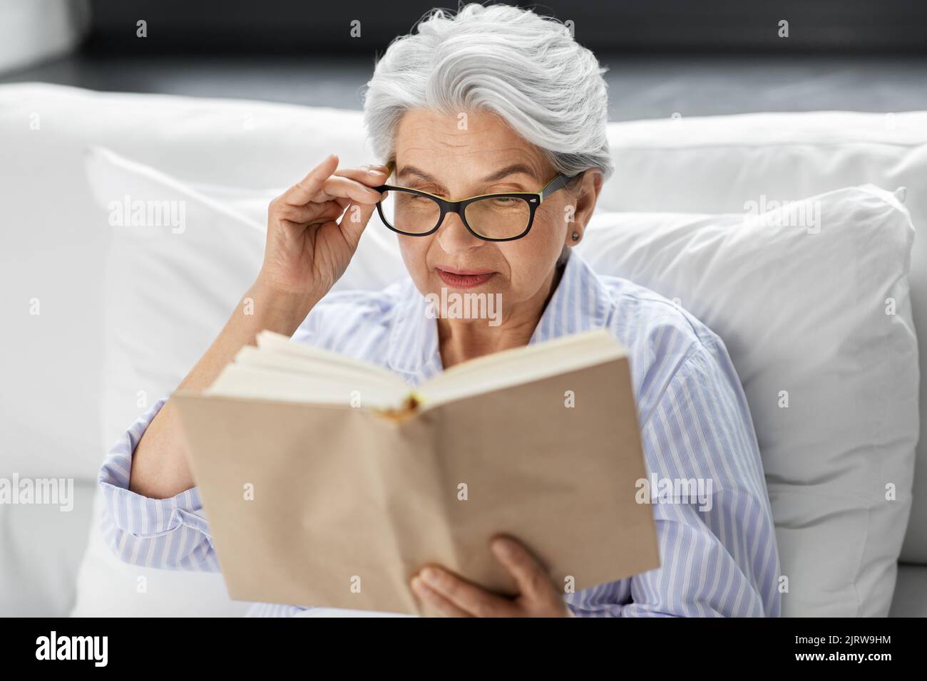 old woman in glasses reading book in bed at home Stock Photo - Alamy