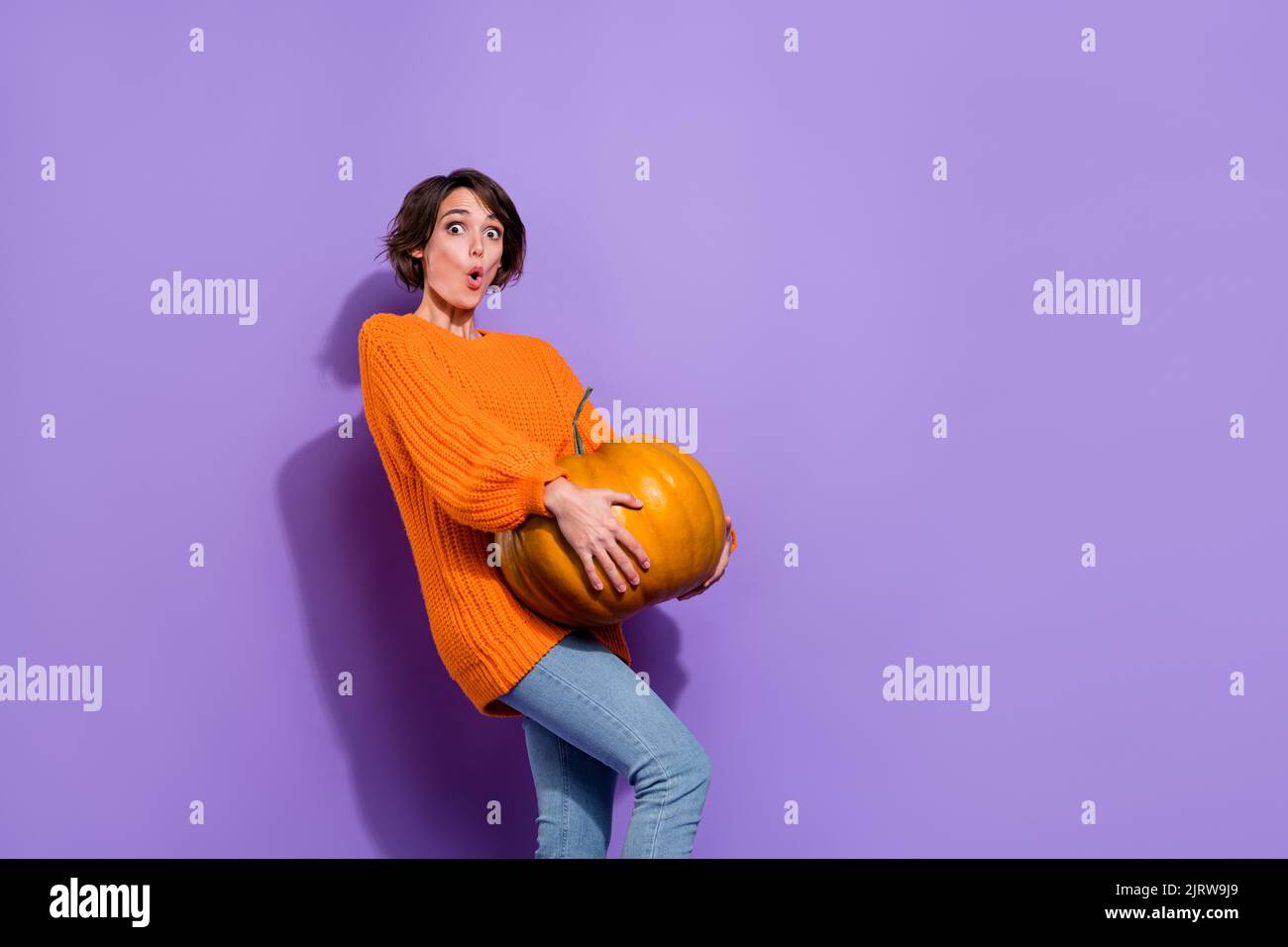 Portrait of attractive funny girly overwhelmed girl carrying heavy big pumpkin isolated over ...
