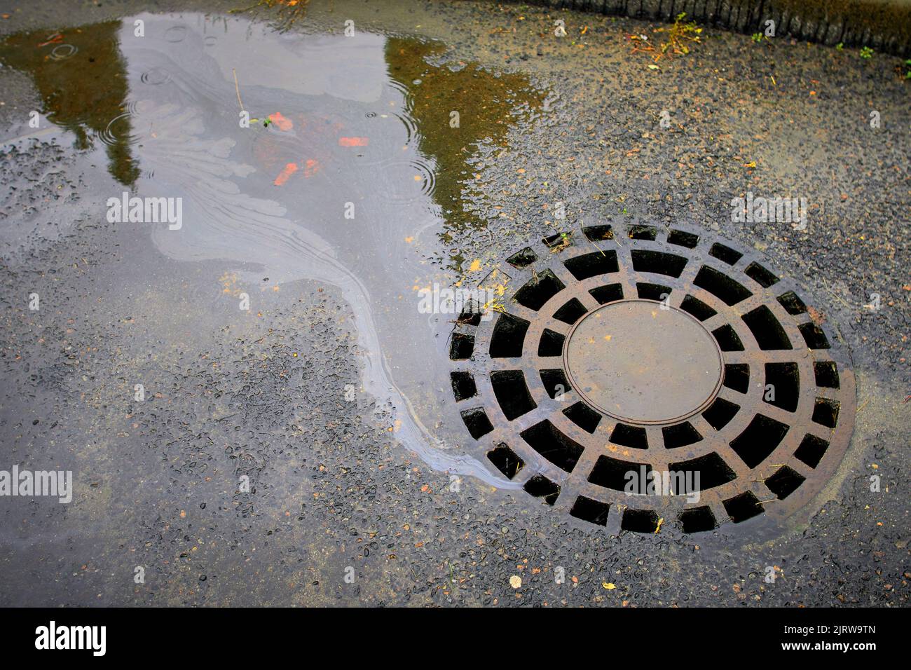 An oil slick on the background of an asphalt road flows into a storm ...