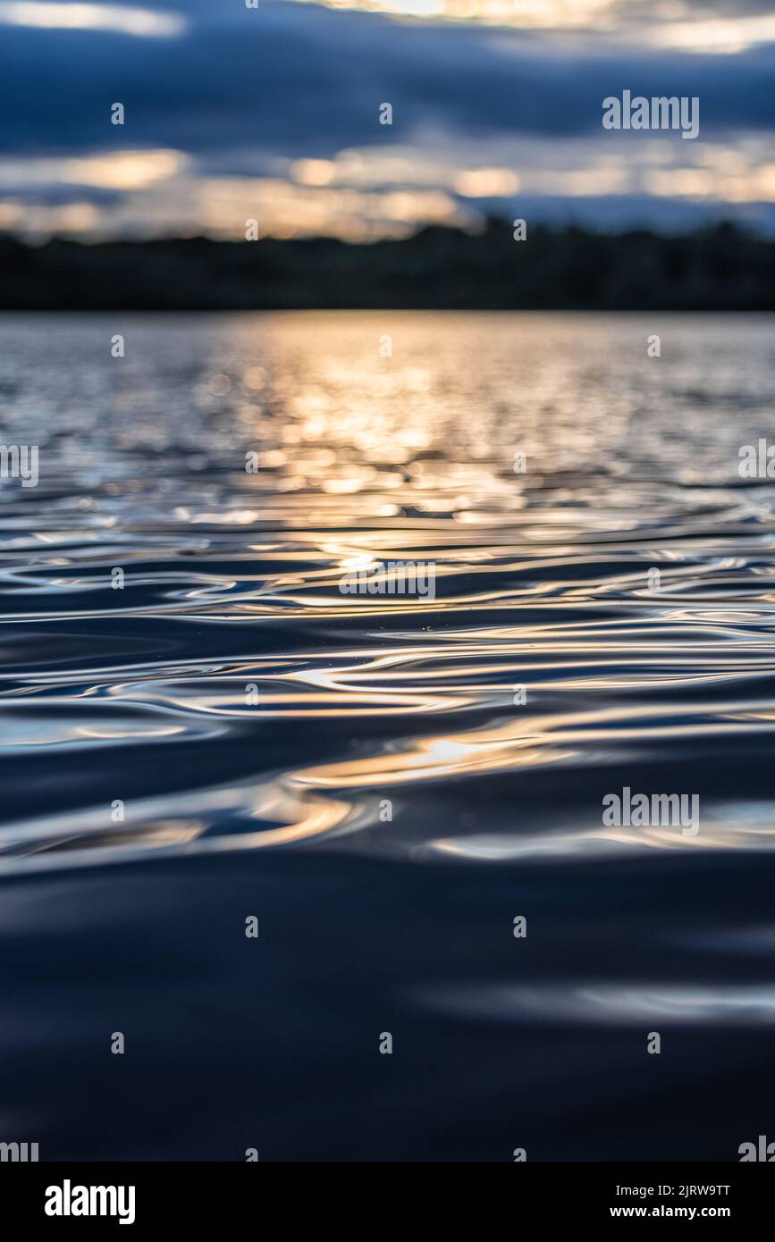 A vertical shot of smooth and calm water ripples with the sunset ...