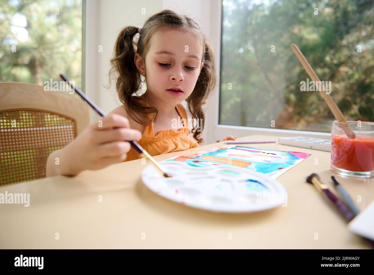 Charming talented little girl, first grader sitting at a table and ...