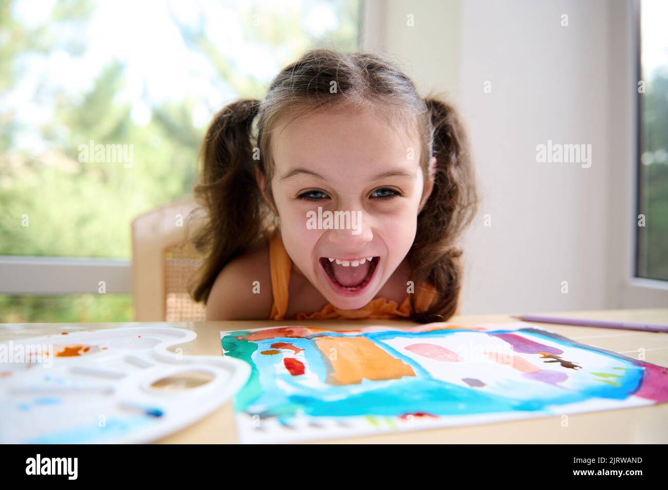 Cheerful funny preschooler little girl grimacing looking at the camera ...