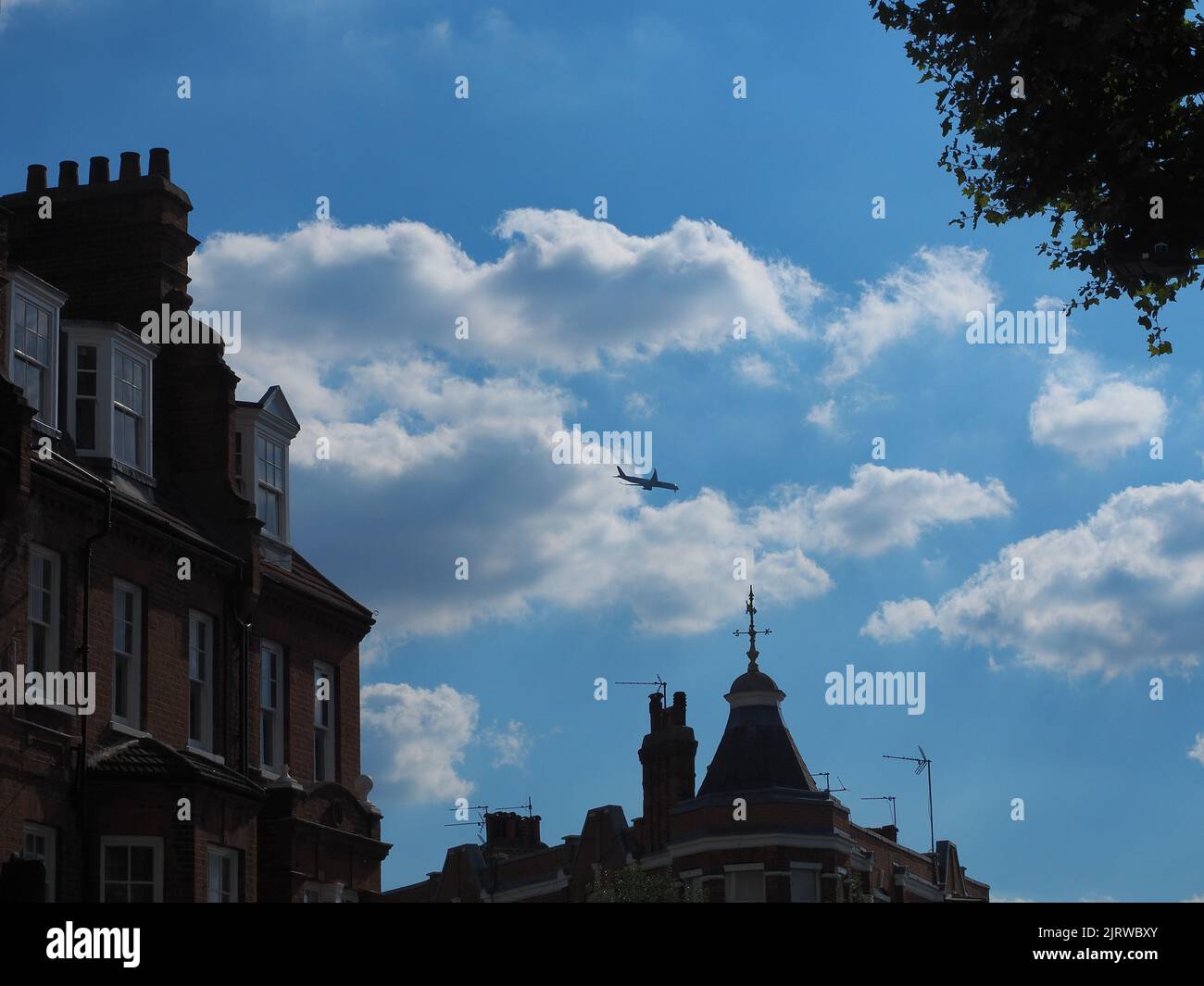 Plane flying over rooftops with clouds in the sky Stock Photo - Alamy