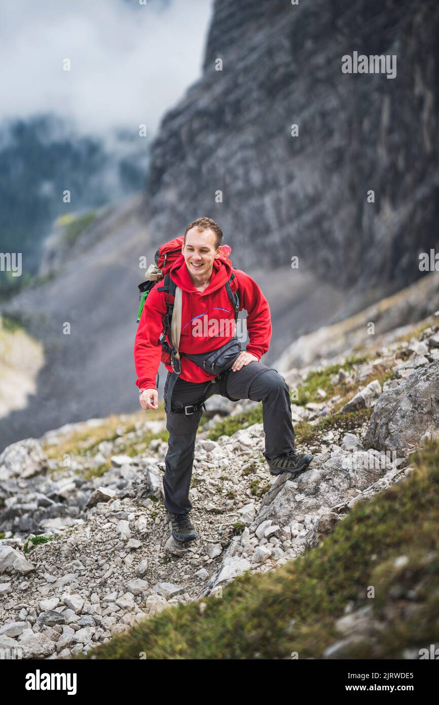 A vertical shot of a climber in a red coat smiling and going up the ...