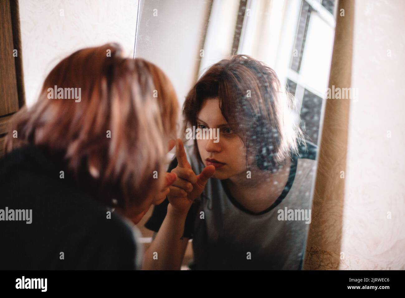 Young woman touching her reflection while looking in the mirror at home ...