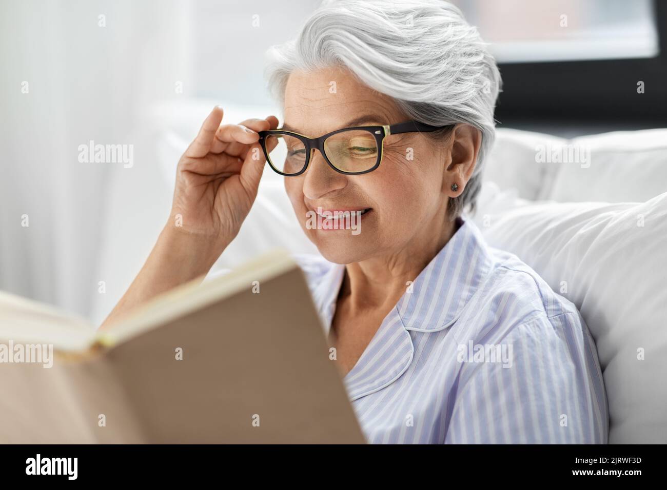 old woman in glasses reading book in bed at home Stock Photo - Alamy