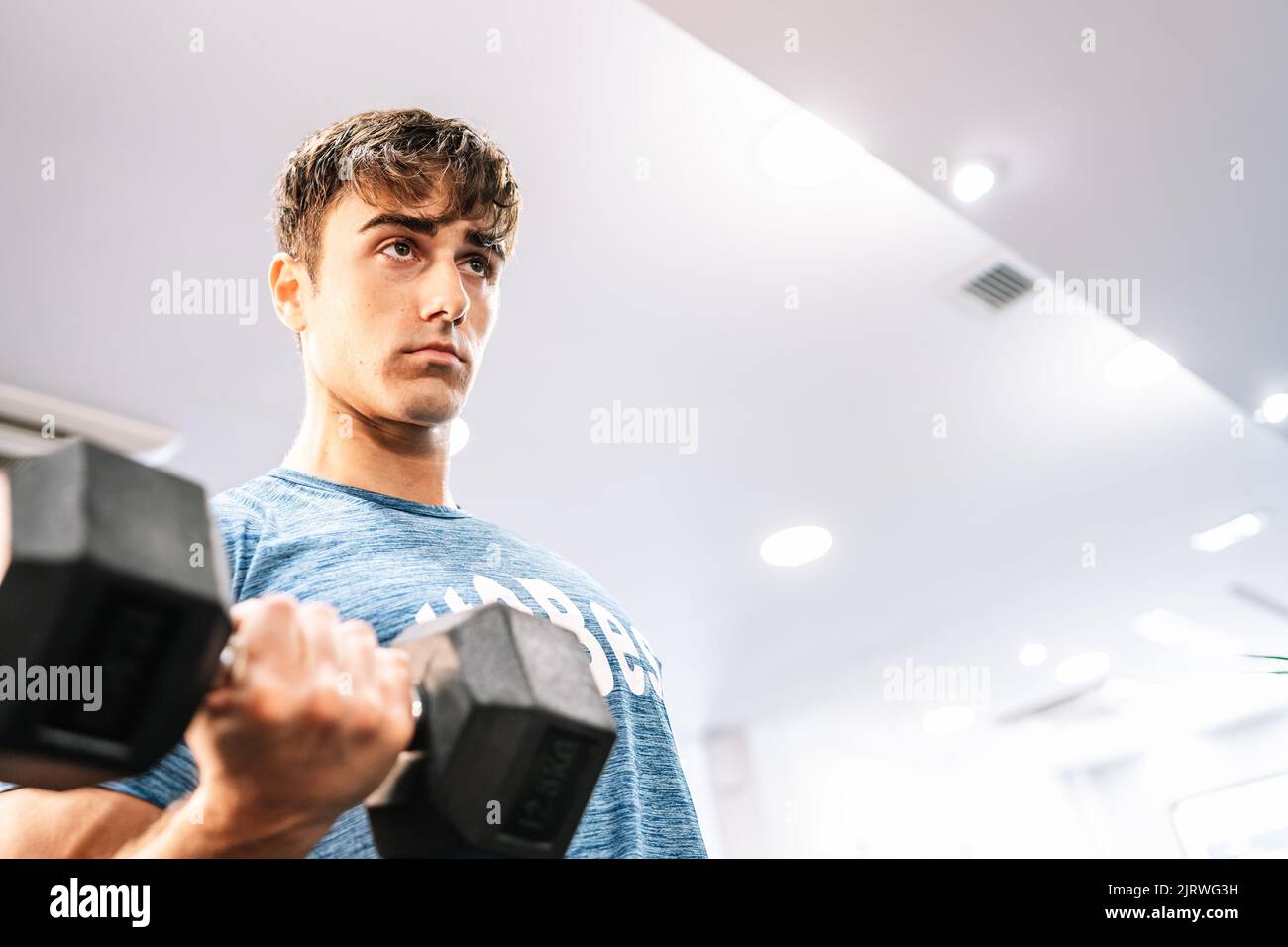 From below determined young sportsman doing bicep curl exercise with ...
