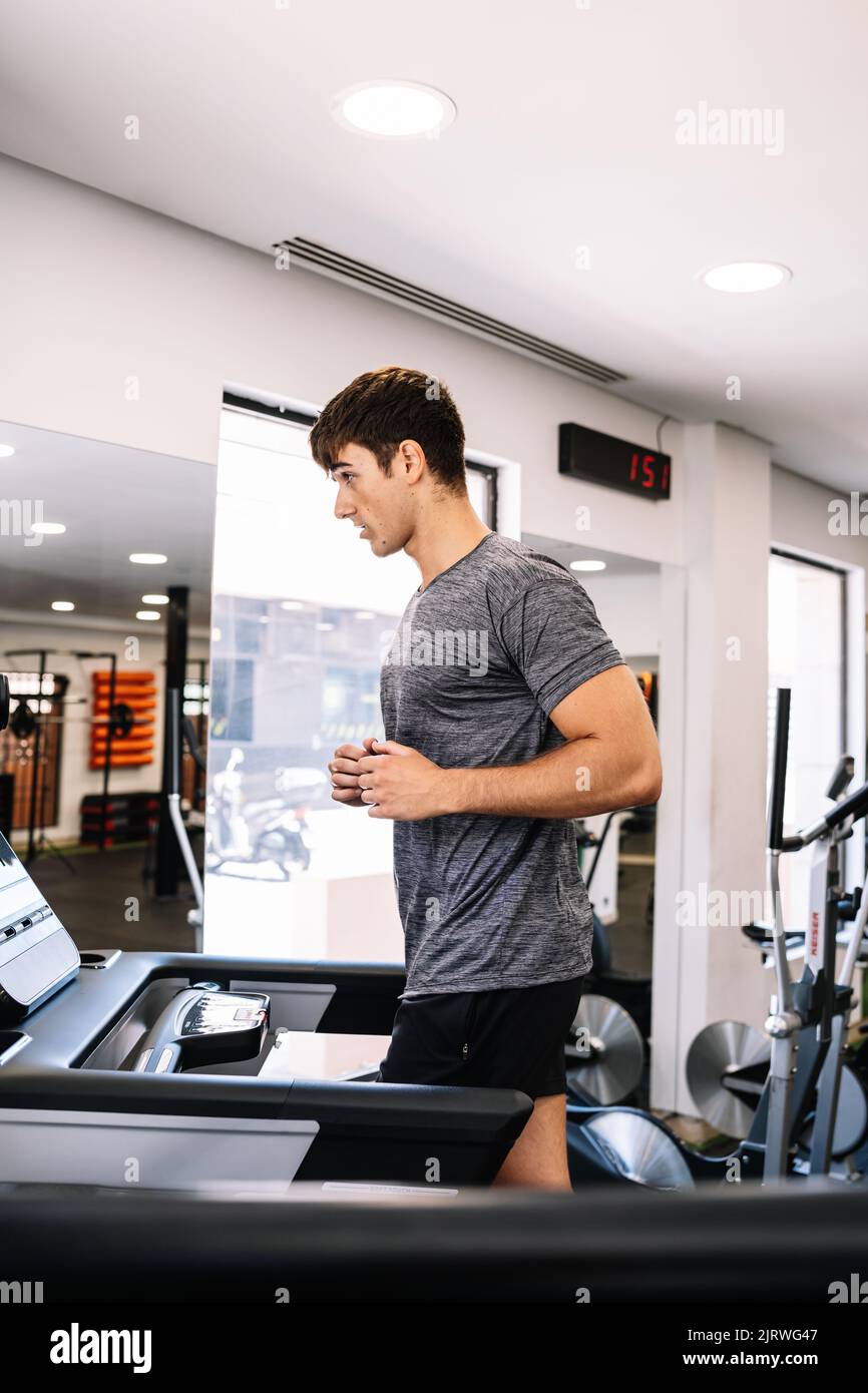 Side view of focused young sportsman in activewear running on treadmill ...