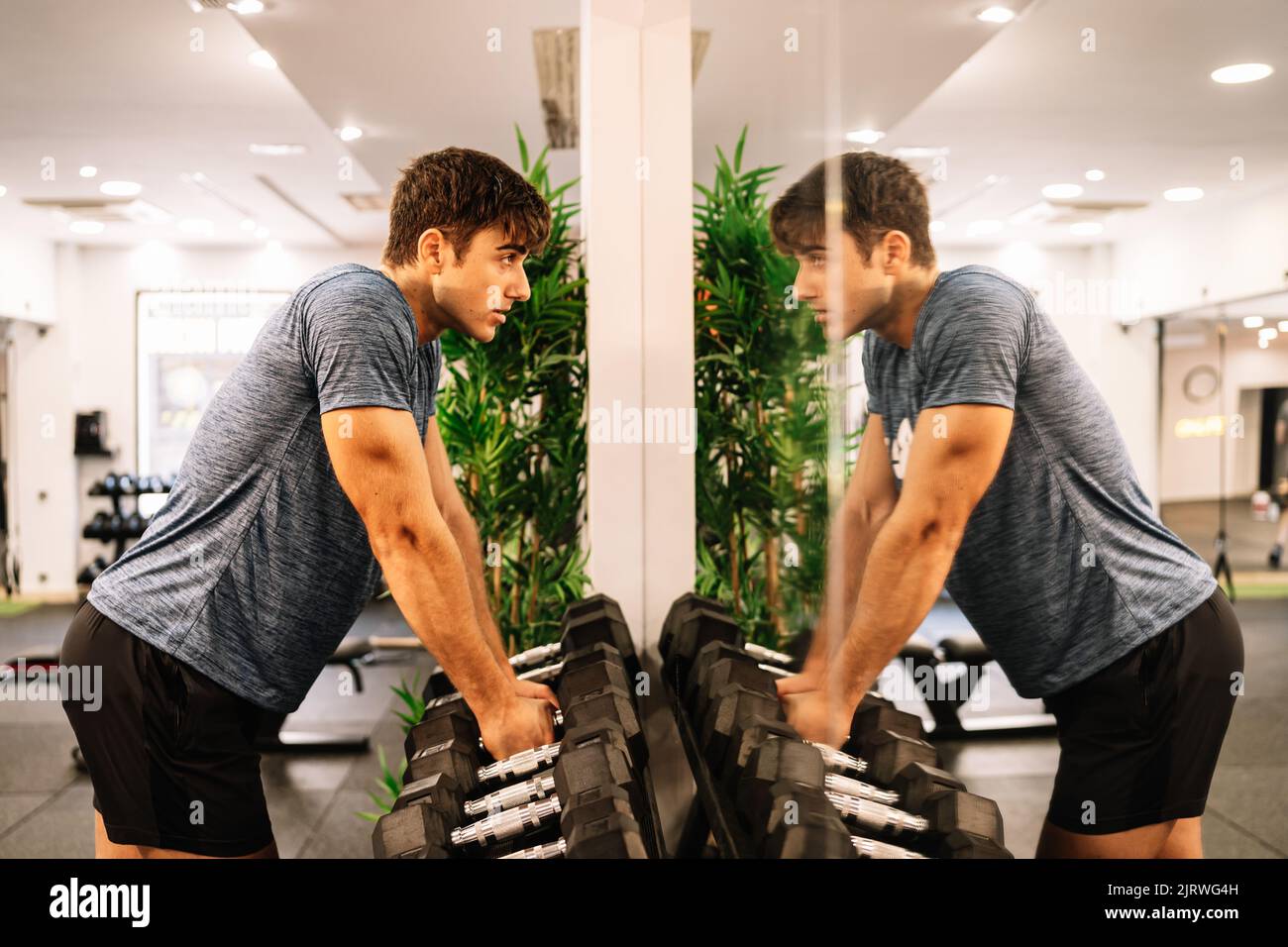 Side view of sportsman in gray shirt taking heavy dumbbells from rack ...
