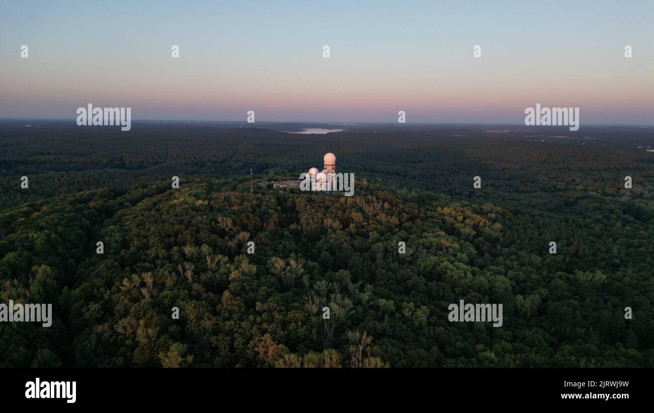 An aerial view of Teufelsberg surrounded by lush trees with a cloudless ...