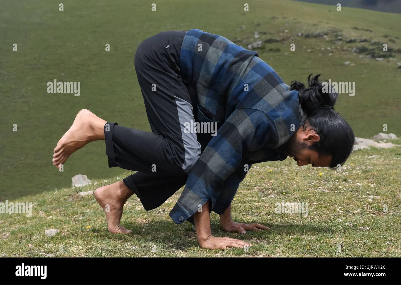 Side view of a young man hiker trying to do Bakasana Yoga Pose (Crow ...