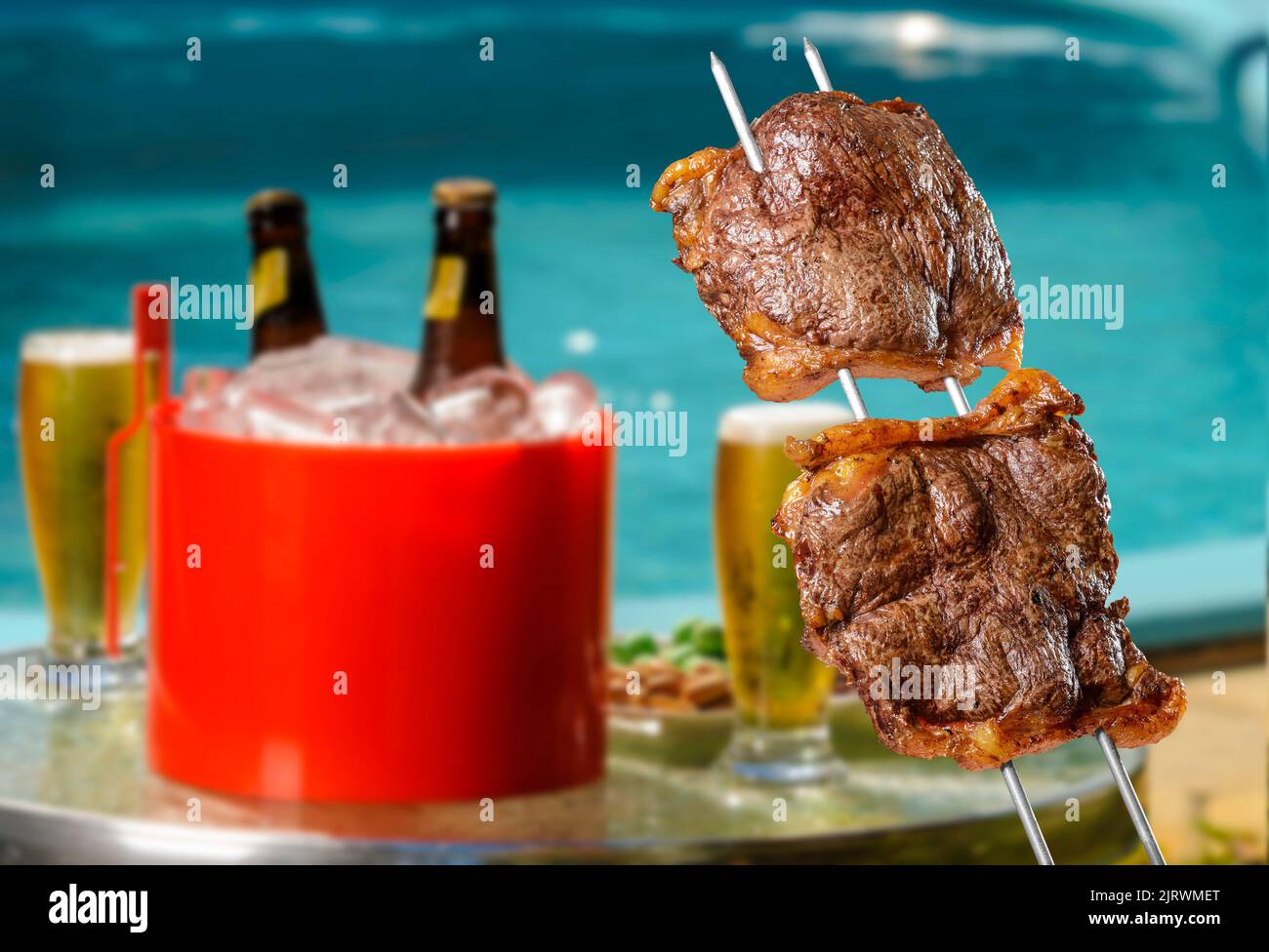 Brazilian barbecue picanha on skewers with blurred beers and pool in ...