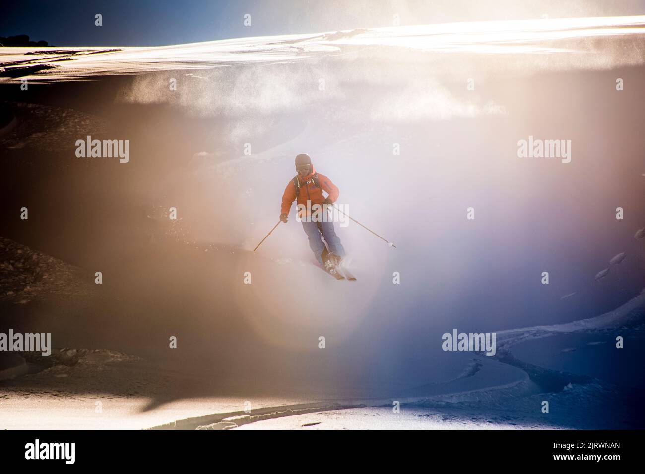 Single off piste skier descends fresh powder snow slope with sun behind ...