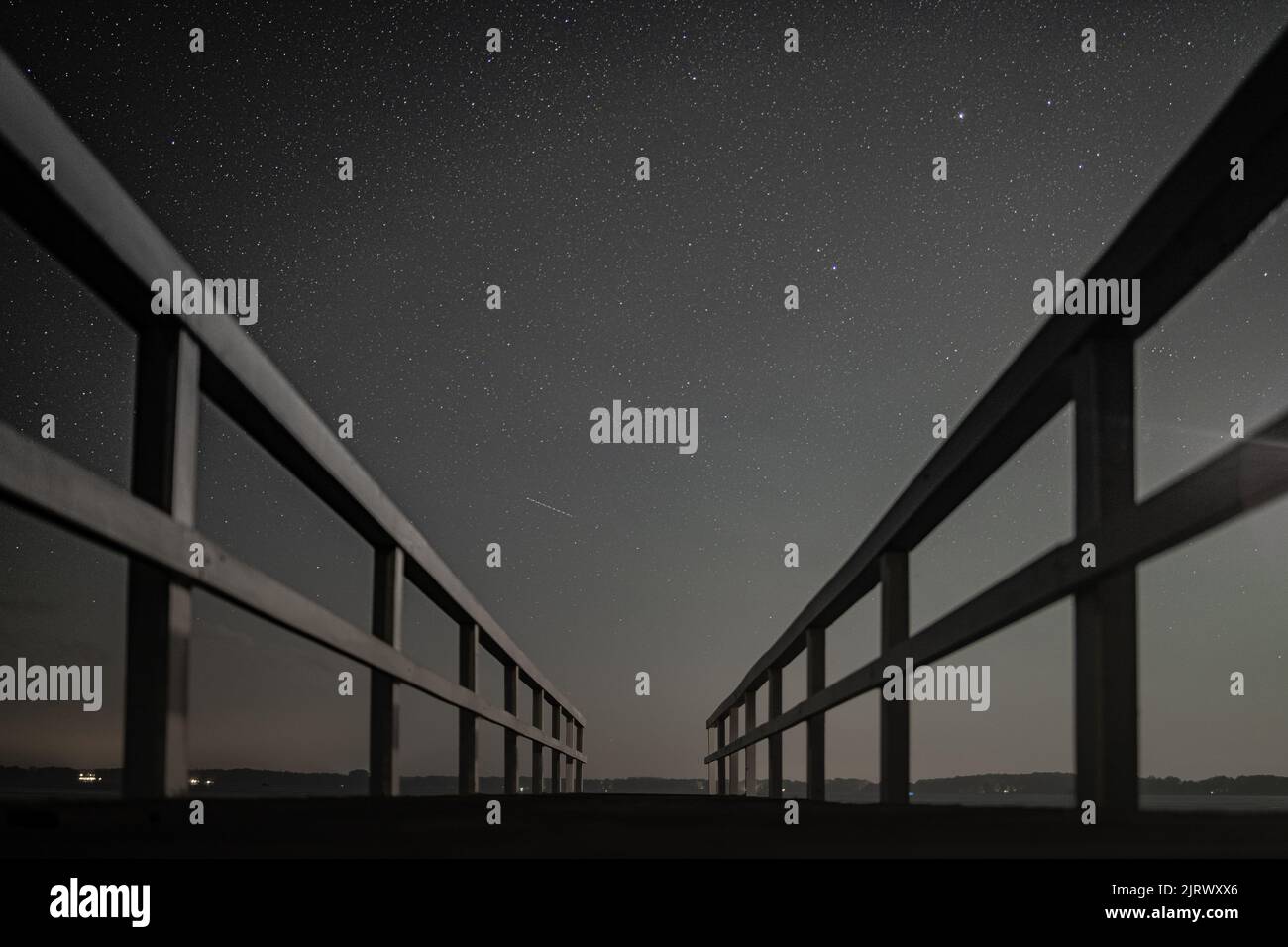 The low-angle grayscale of a fenced pathway under the starry night sky ...