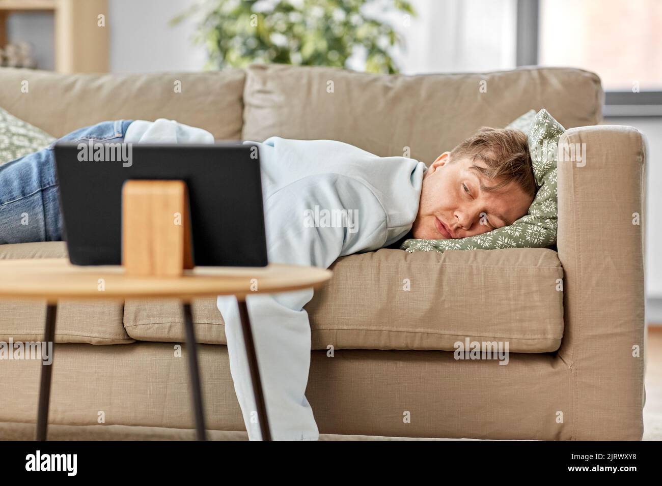 bored man with tablet pc lying on sofa at home Stock Photo - Alamy