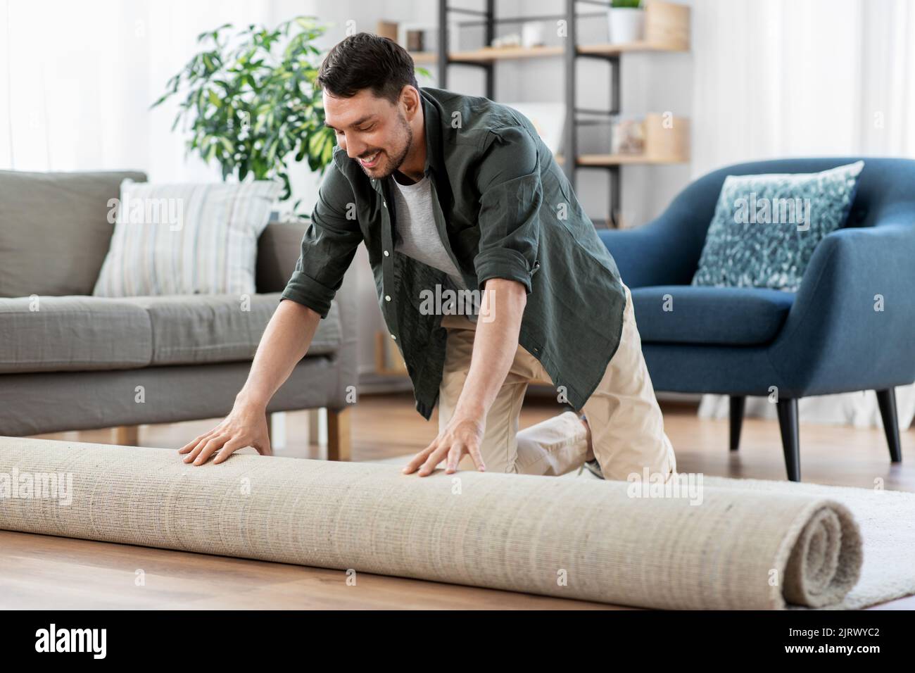 happy smiling young man unfolding carpet at home Stock Photo - Alamy