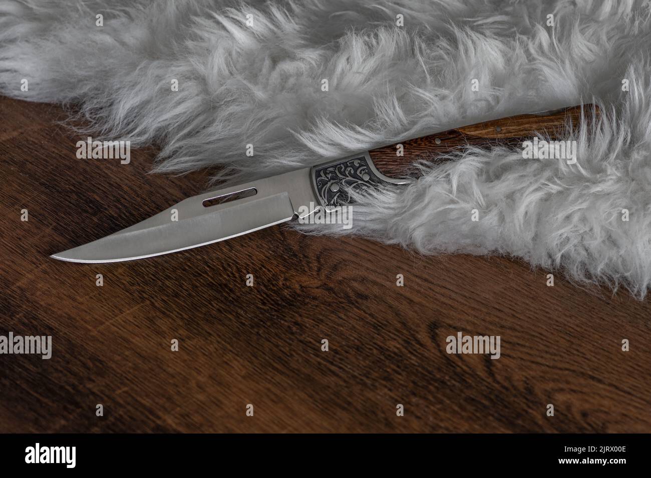 sharp handmade foldable knife with brown wood handle on white sheep fur ...