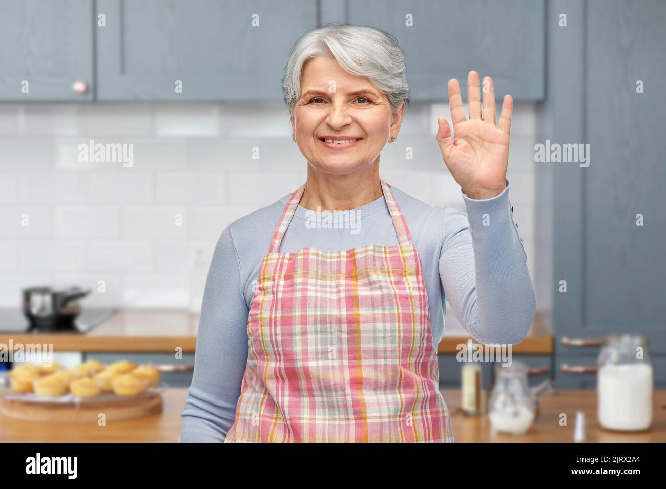 smiling senior woman in apron waving hand Stock Photo - Alamy