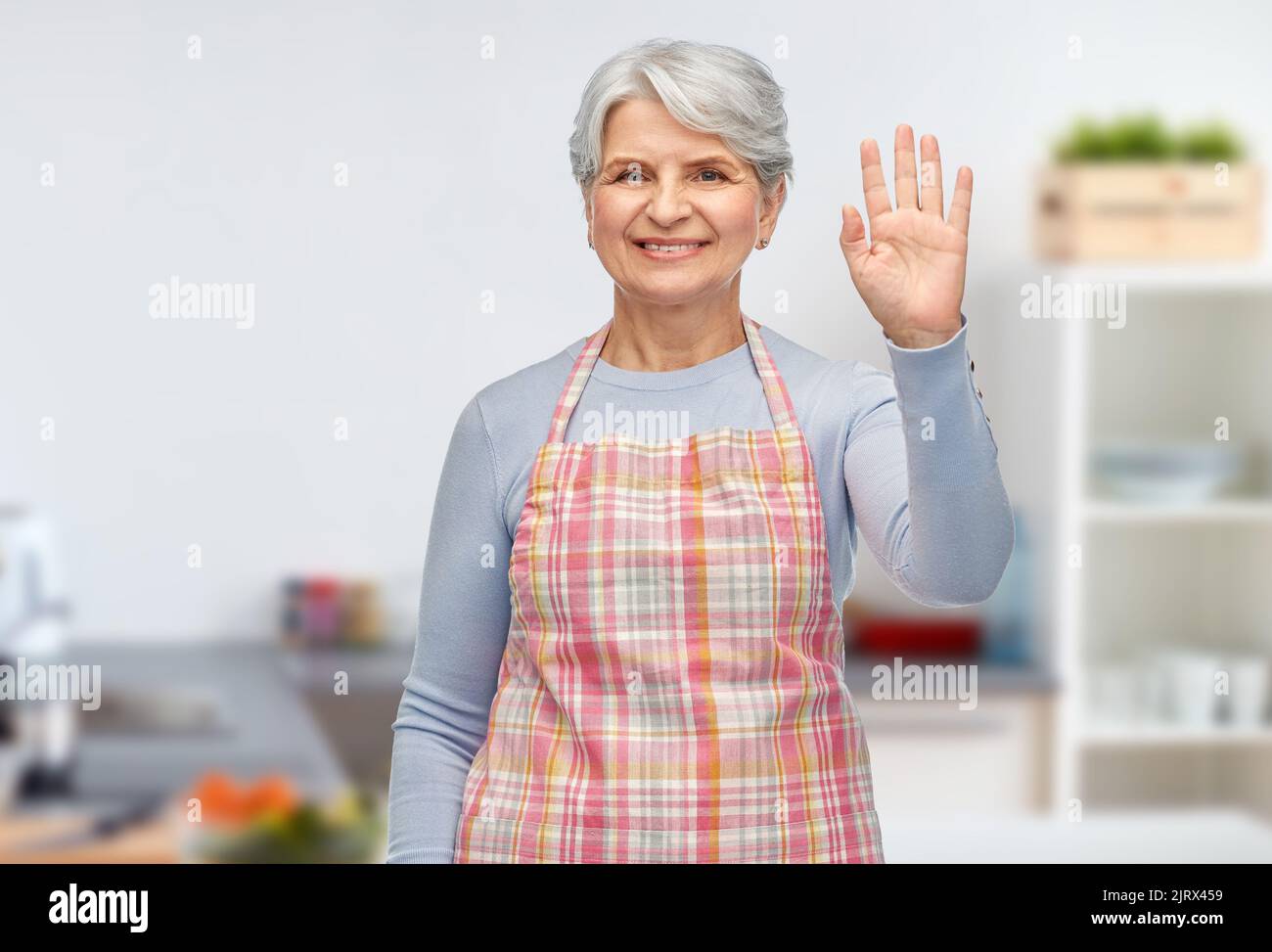 smiling senior woman in kitchen apron waving hand Stock Photo - Alamy