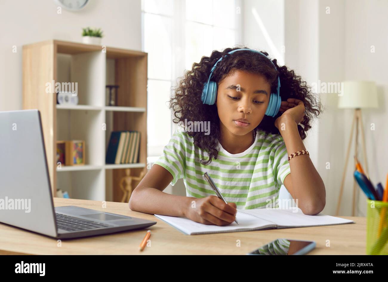 African student girl in headphones sitting at desk, doing homework and ...