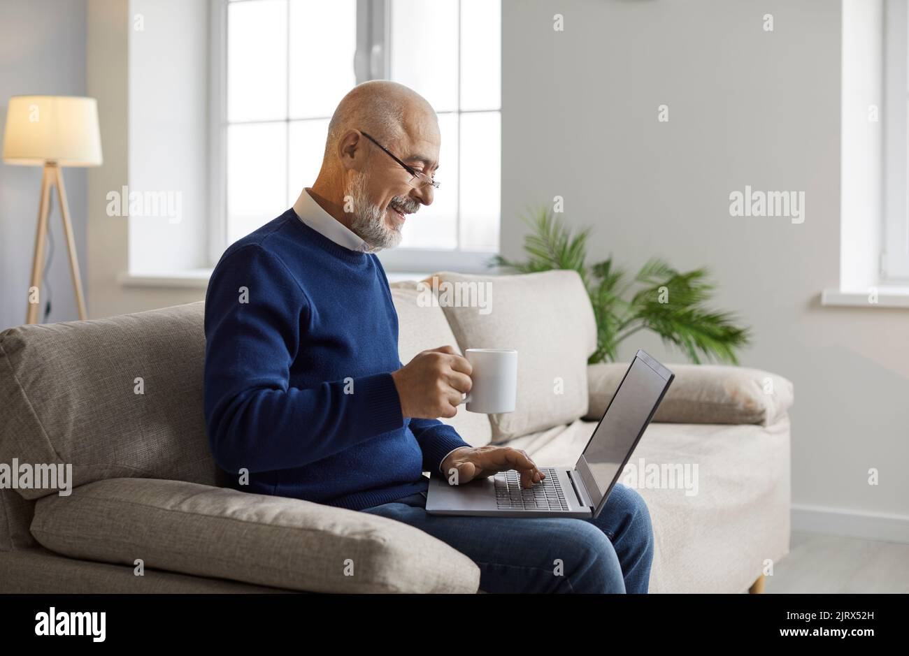 Happy senior man sitting on sofa at home, using laptop computer and ...