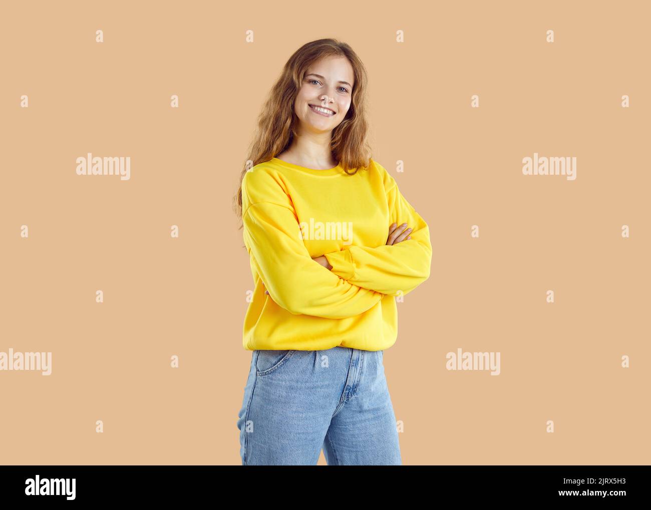 Young smiling woman in yellow sweatshirt and jeans is posing on beige ...