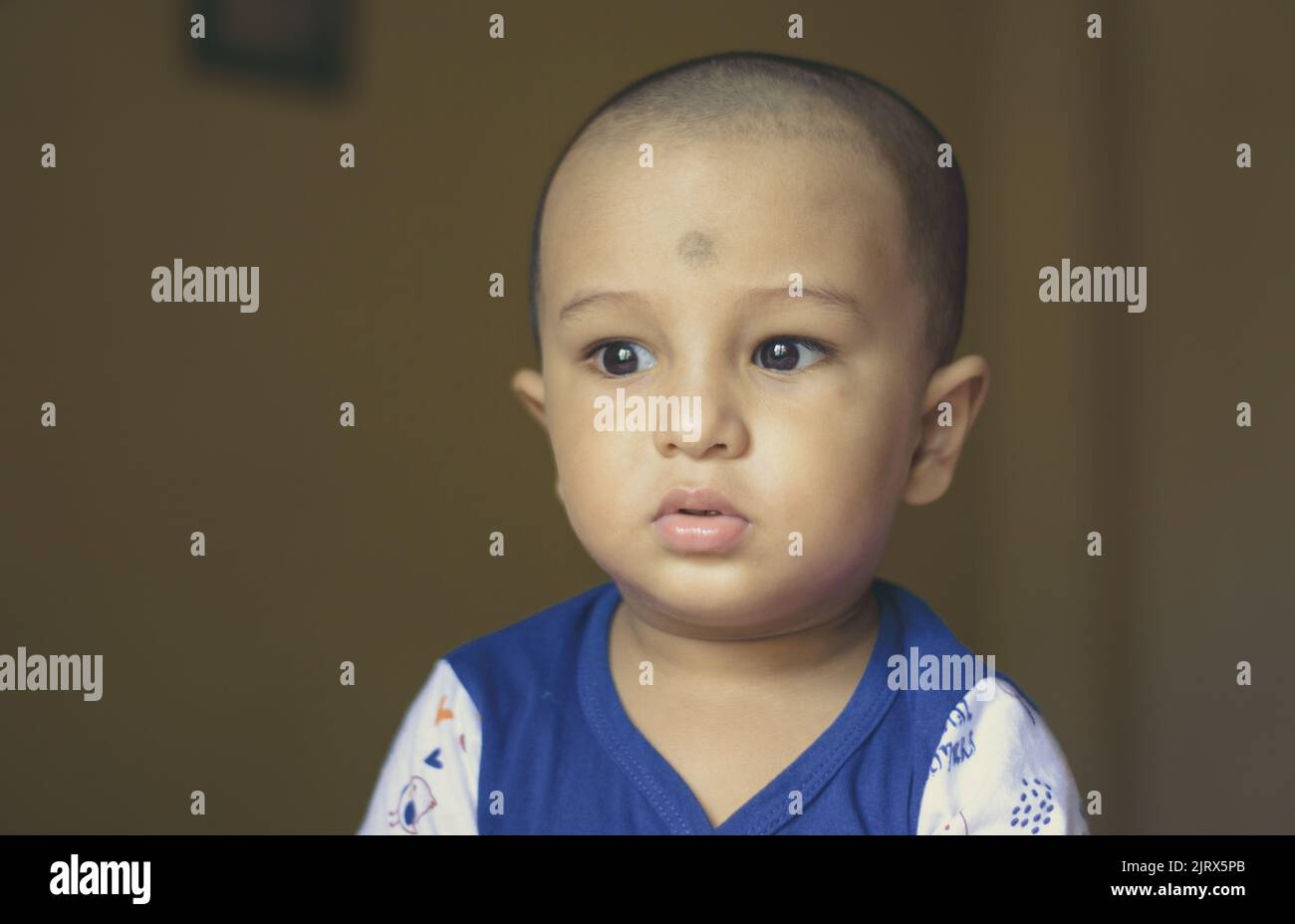 Cute bald indian baby boy in blue and white shirt looking away. Head ...