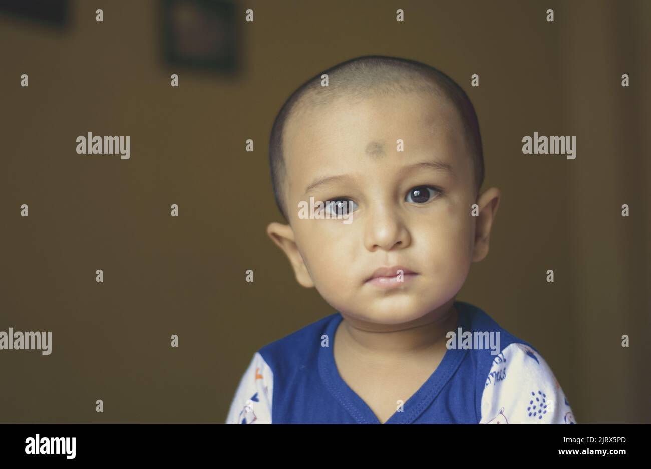 Cute bald indian baby boy in blue and white shirt looking away. Head ...
