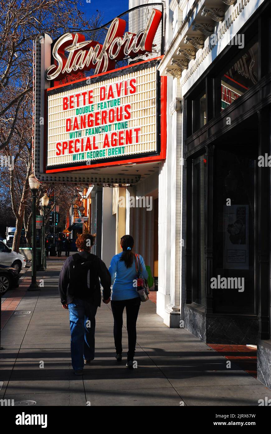 A young adult couple walk while holding hands under a marquee for a ...