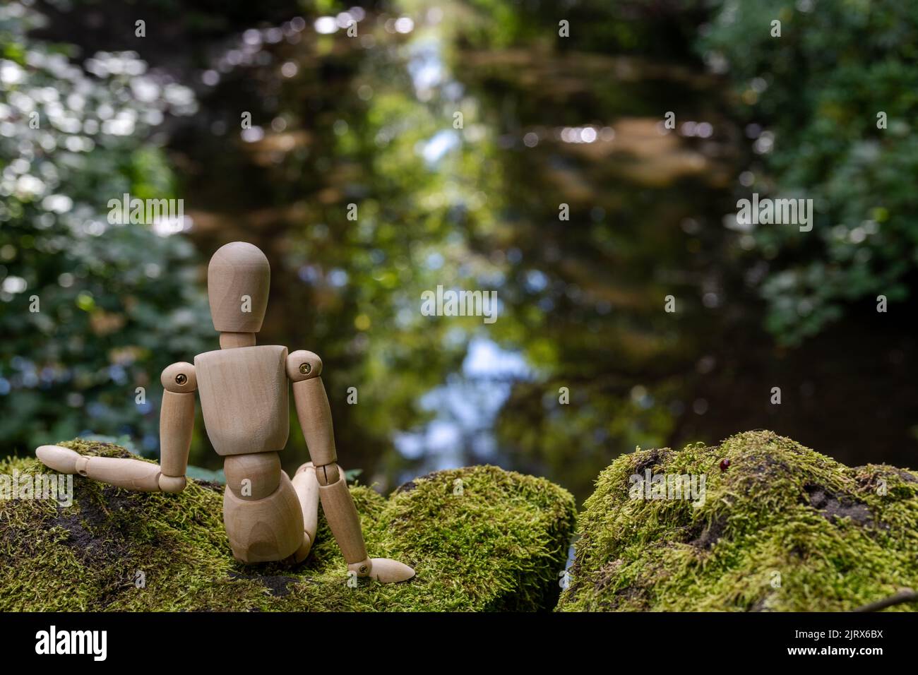 A wooden artist's figure sitting, looking down into a river. Concept of ...