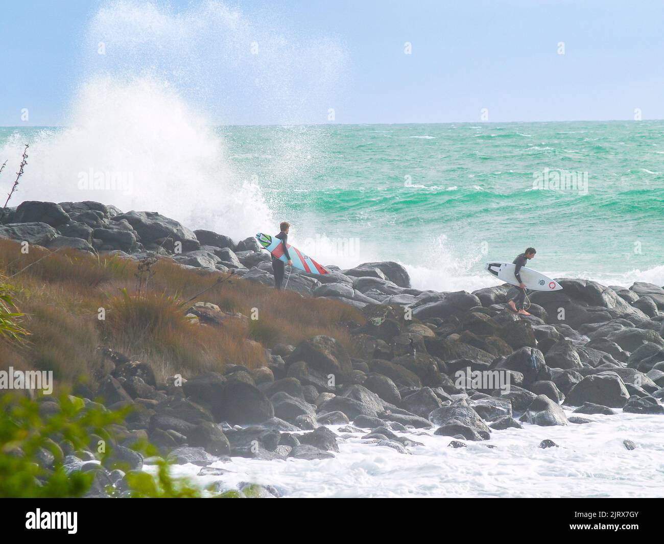 Raglan, New Zealand -June 7 2008 young male surfers clamber over rocky ...