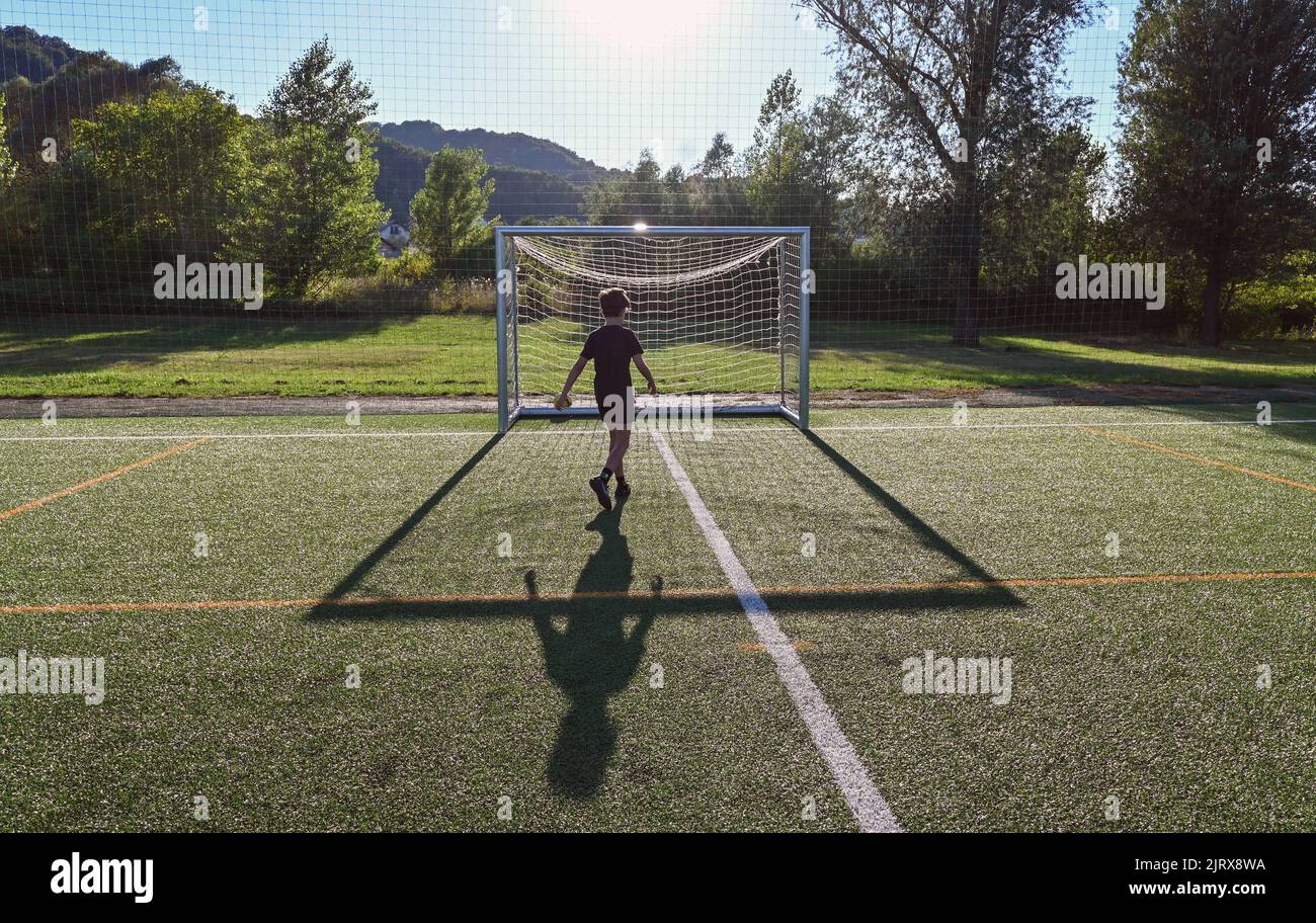 Young boy playing soccer on the football field at sunset, shooting at ...