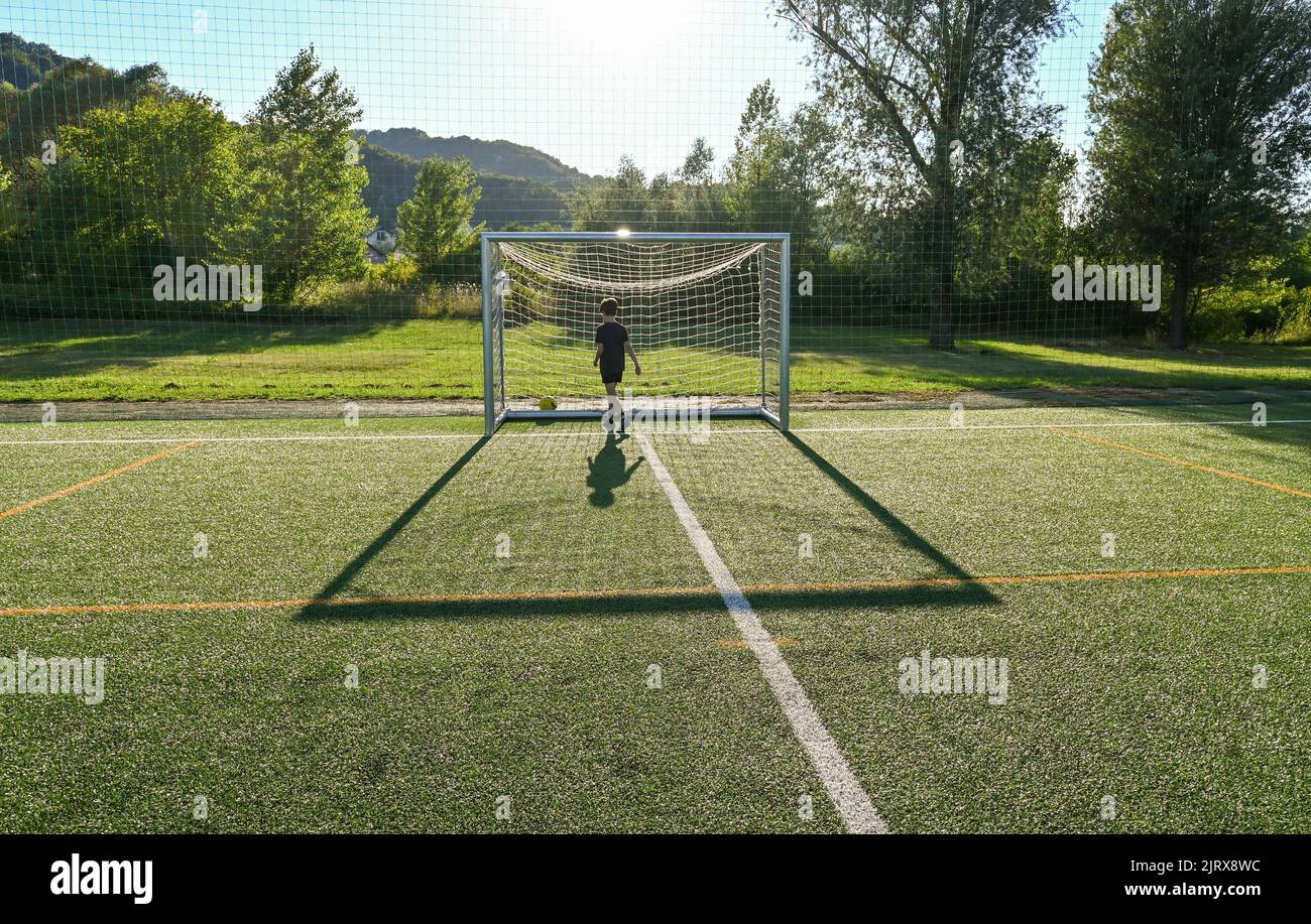 Young boy playing soccer on the football field at sunset, shooting at ...