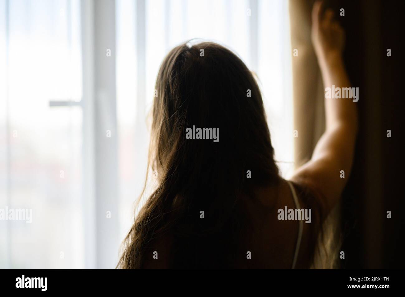 Happy woman opening window curtains at home, back view. Good morning ...