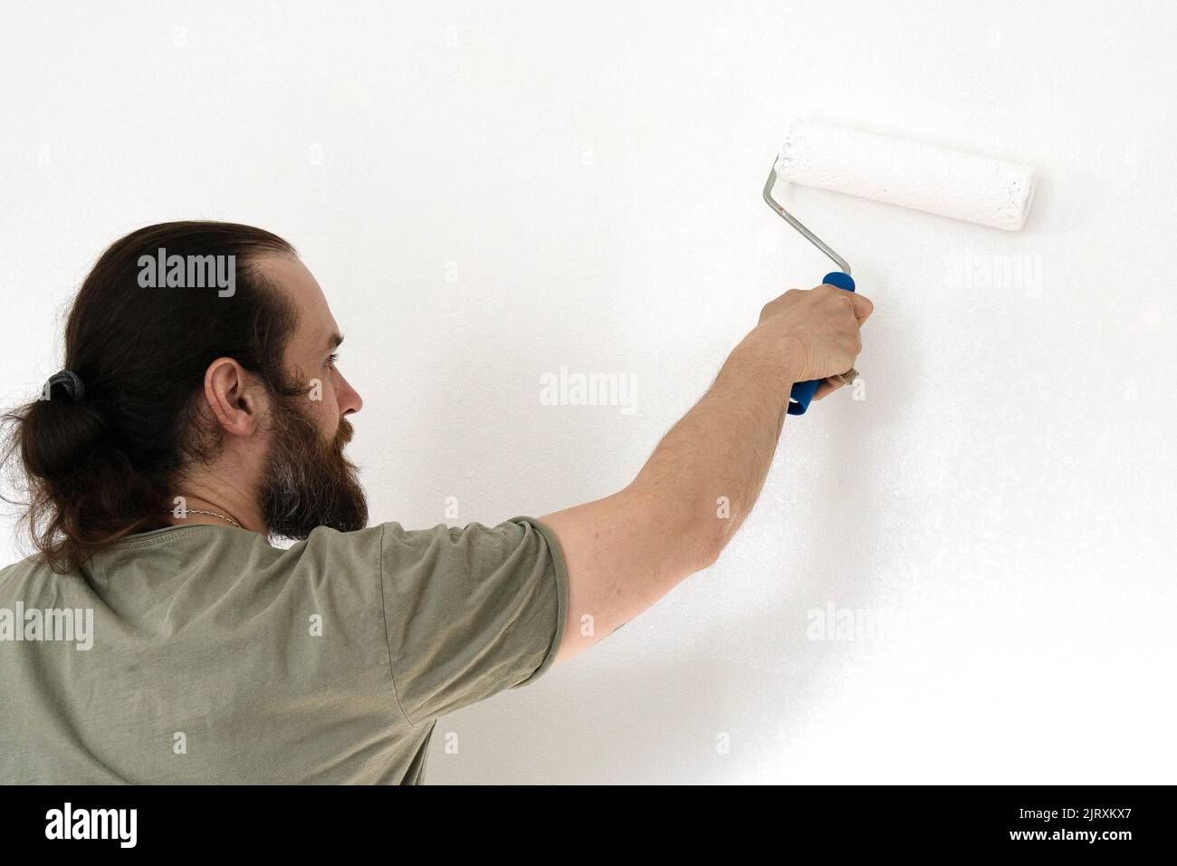 Back of young caucasian man painting white wall with paint roller for ...
