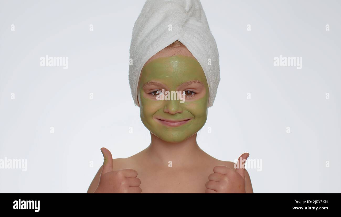 Beautiful young smiling child girl in towel on head applying cleansing ...