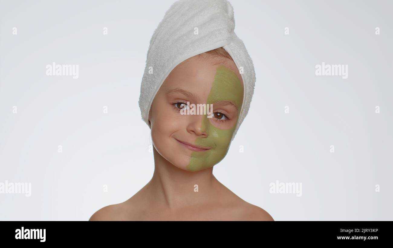 Beautiful young smiling child girl in towel on head applying cleansing ...