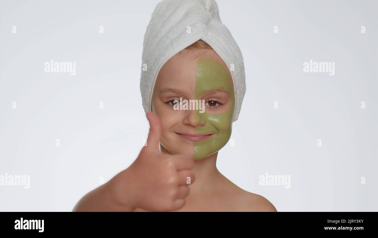 Beautiful young smiling child girl in towel on head applying cleansing ...