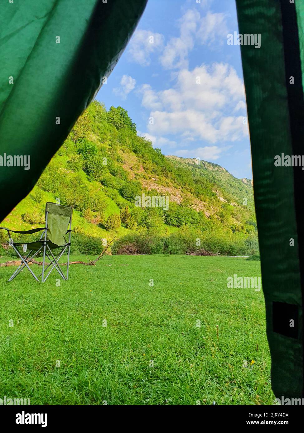 The mountain greenery view with a folding chair from a tent, vertical ...