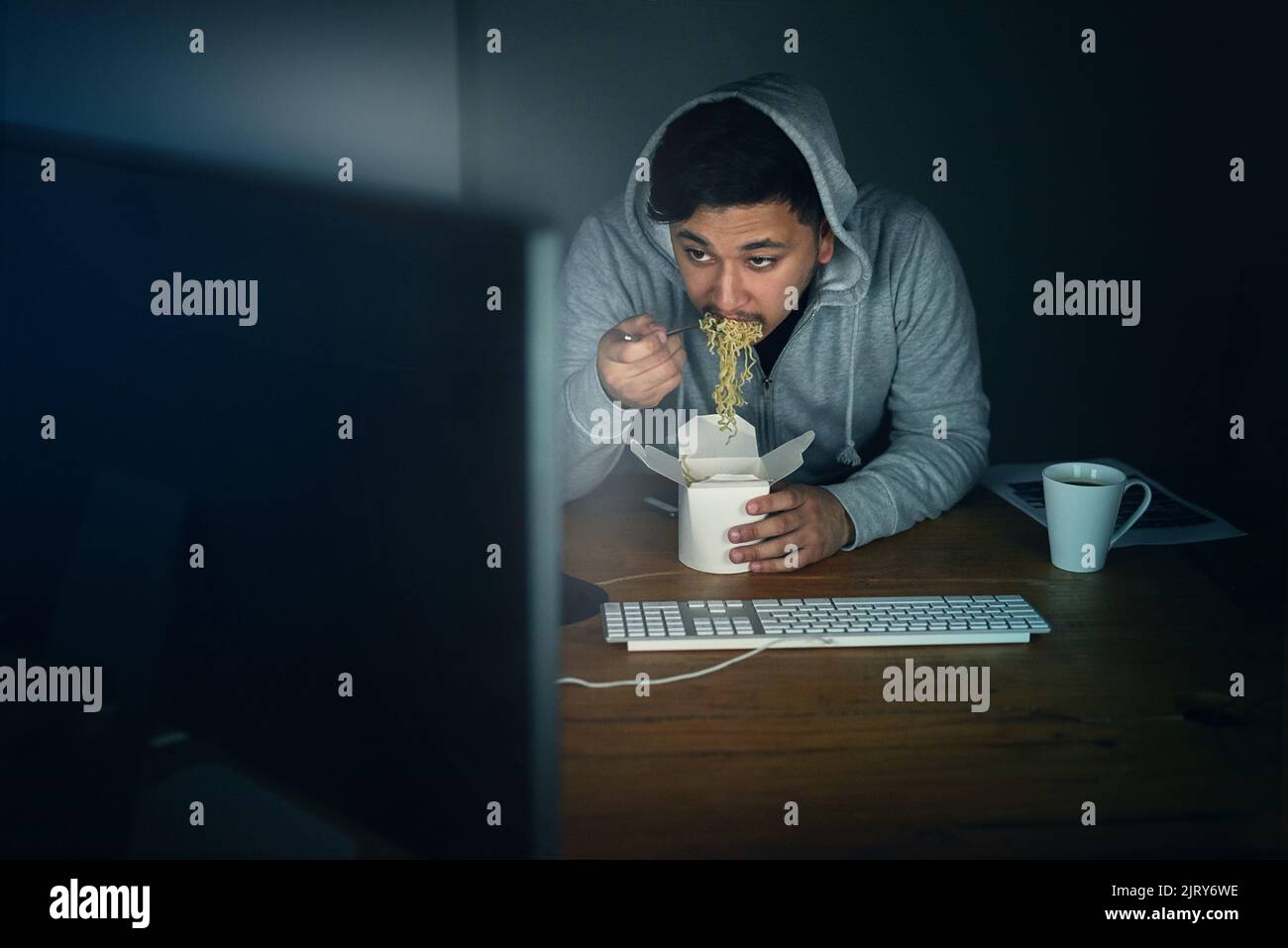 Fuelled by noodles. a young man eating takeaway while working at his ...